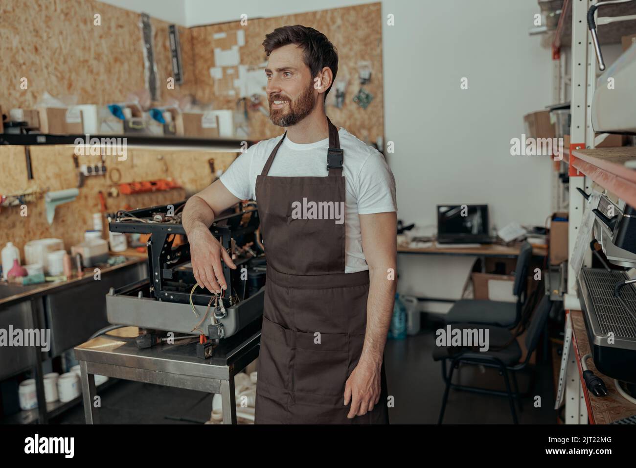 Repairman in uniform standing on workshop of coffee machines warehouse ...