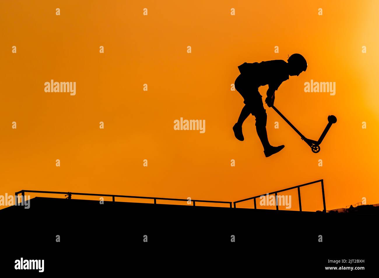 Teenager silhouette showing high jump tricks on scooter against orange ...