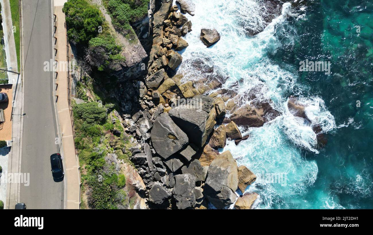 An aerial view of blue sea waves hitting the rocky shore near a road ...