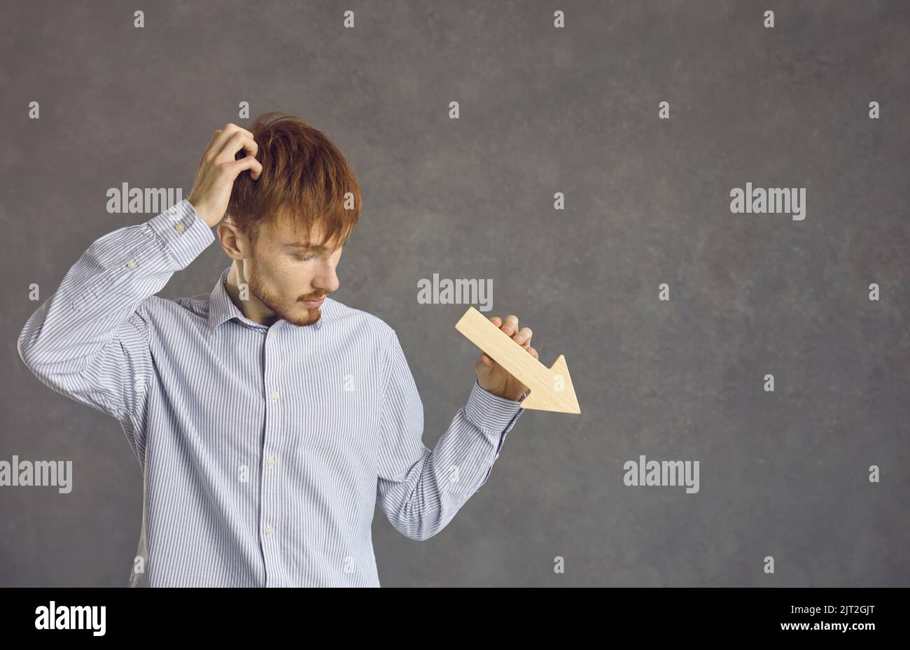 Young man with a puzzled expression looks at a wooden arrow in his ...