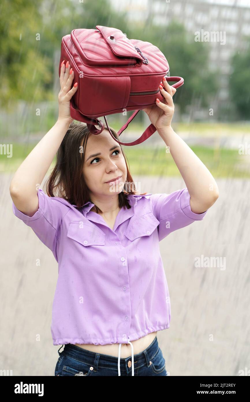 Young woman on street in rain. Positive female in purple shirt holding ...