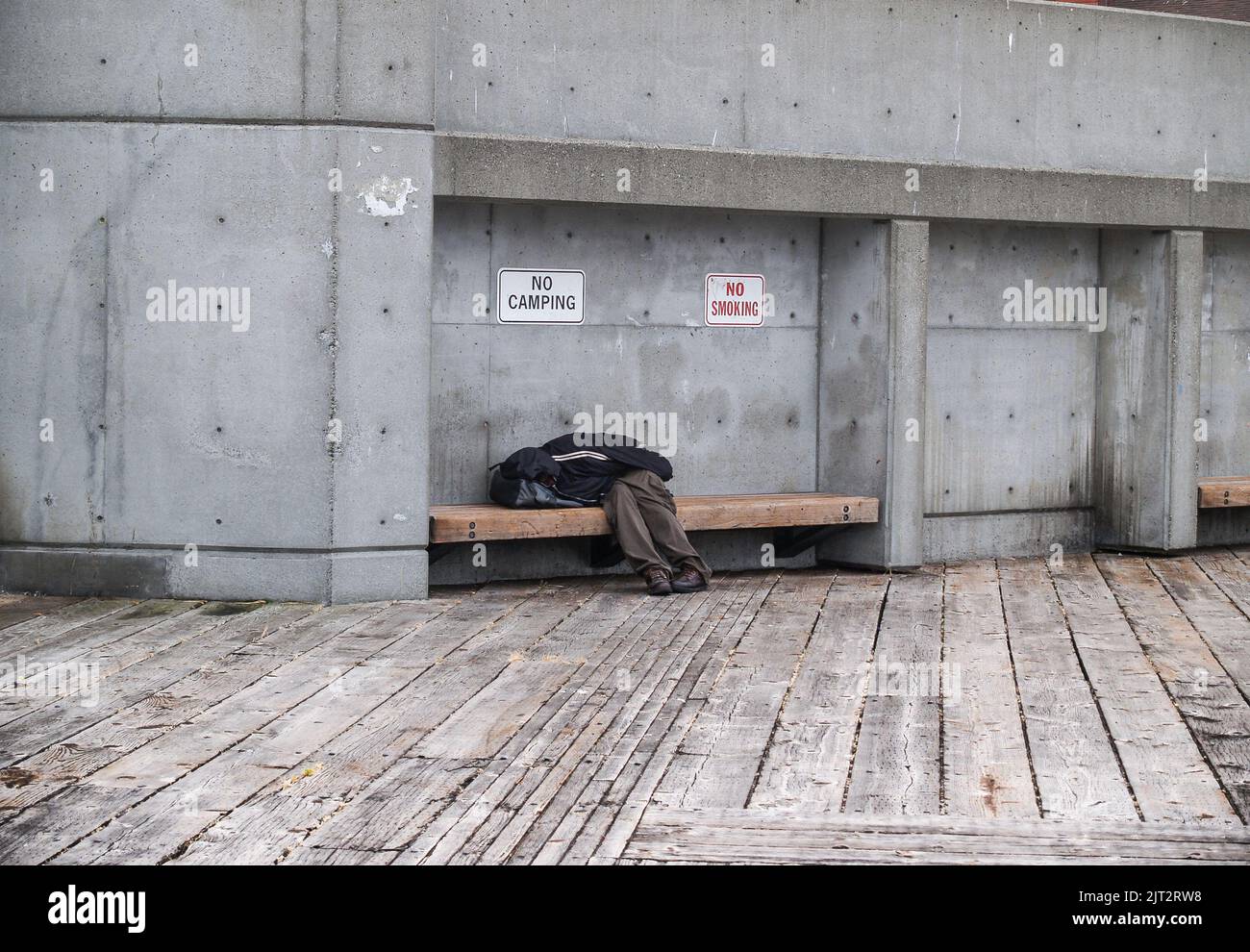 Poverty in city man asleep hiding under clothing on bench with signs ...