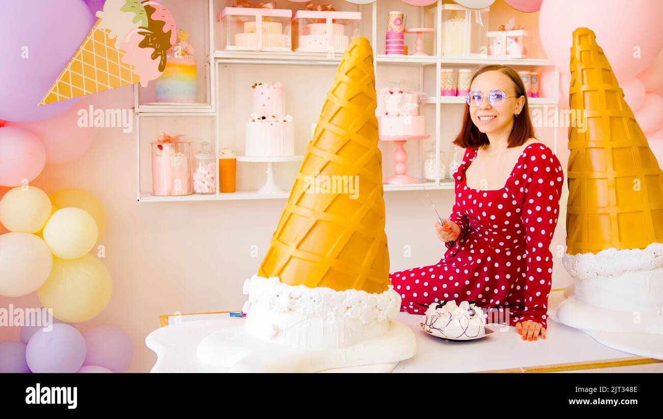 Young woman in red dress sitting on table, cutting cake with knife in ...