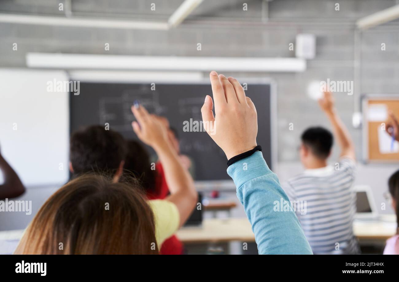 Rear view of a student in the classroom raising her hand to ask a ...