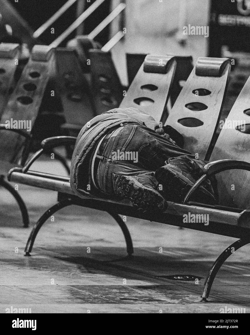 A grayscale of a homeless person sleeping on the station chairs Stock ...