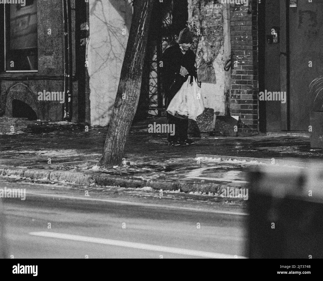 A grayscale of a homeless man walking on the street with bags in hand ...