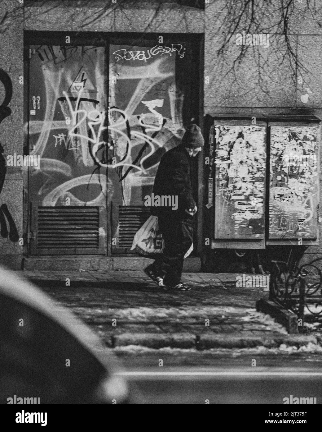 A grayscale of a homeless man walking on the street with bags in hand ...