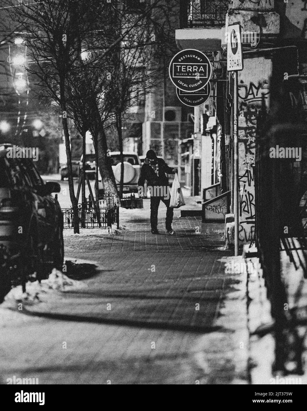 A grayscale of a homeless man walking on the street with bags in hand ...