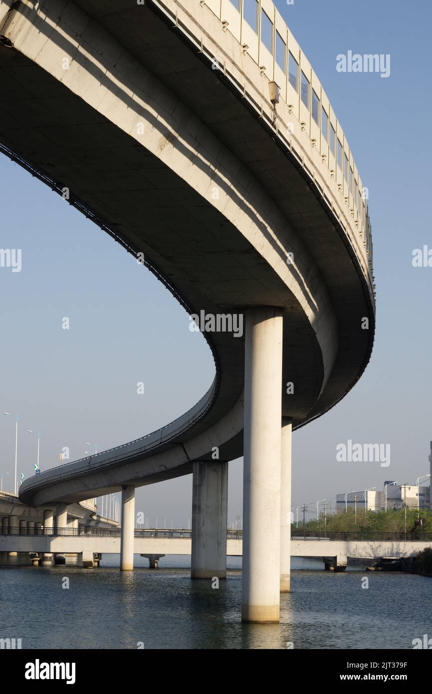 A vertical shot of a curved bridge on water with a blue skyscape in the ...