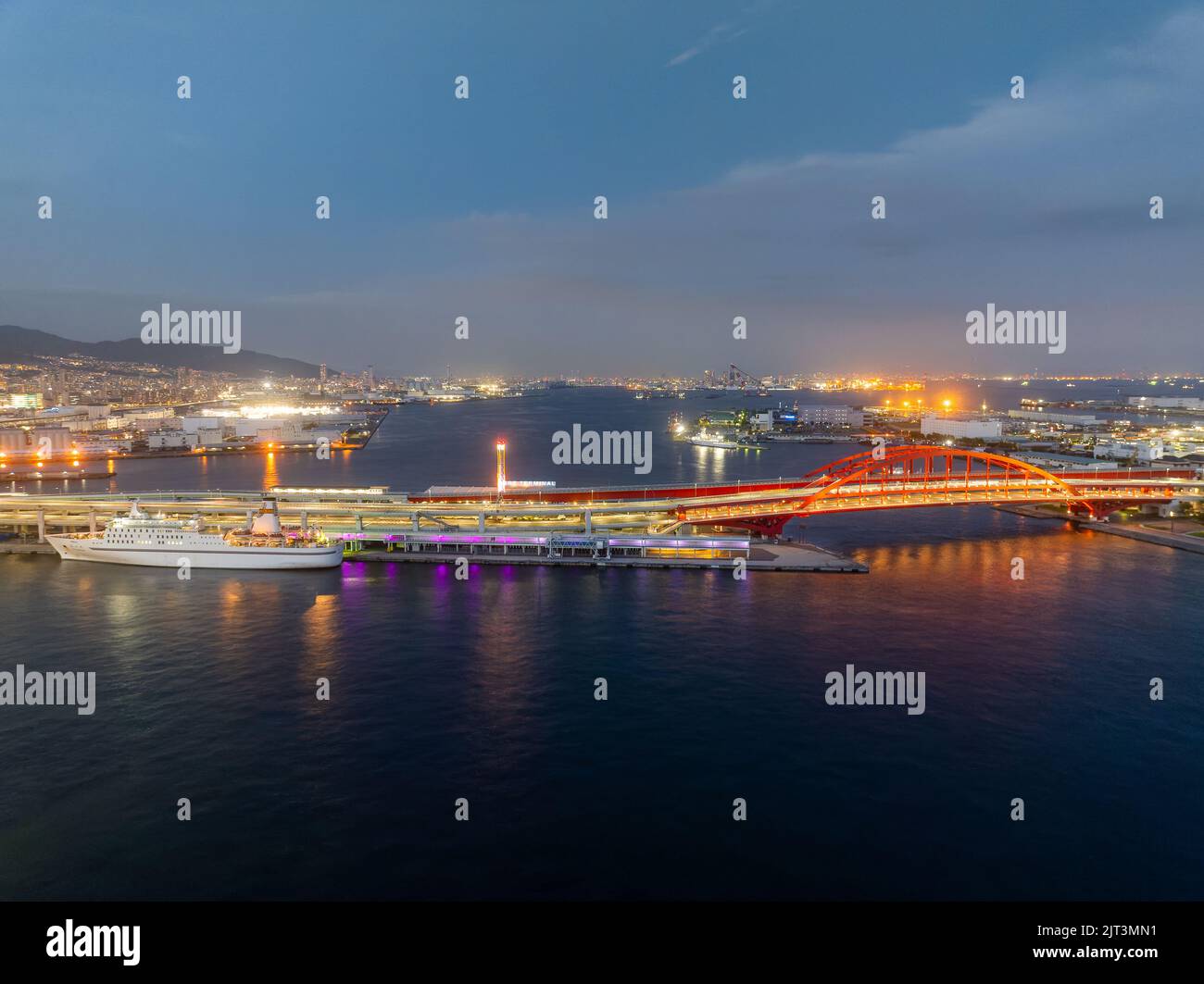 Passenger ferry docked along red arched bridge and city lights at night ...