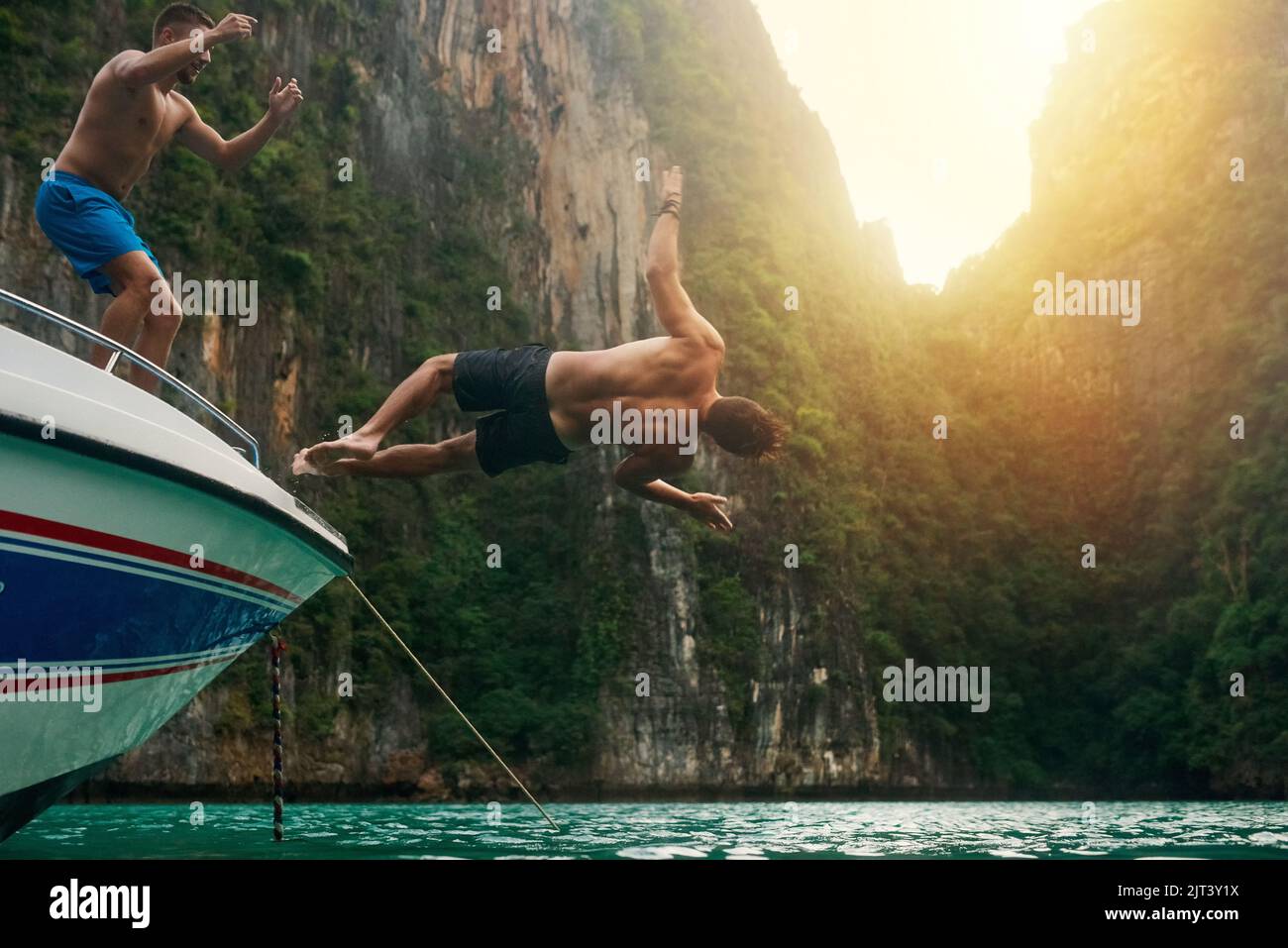 Diving into holiday mode. a young man doing a backflip off a boat while ...