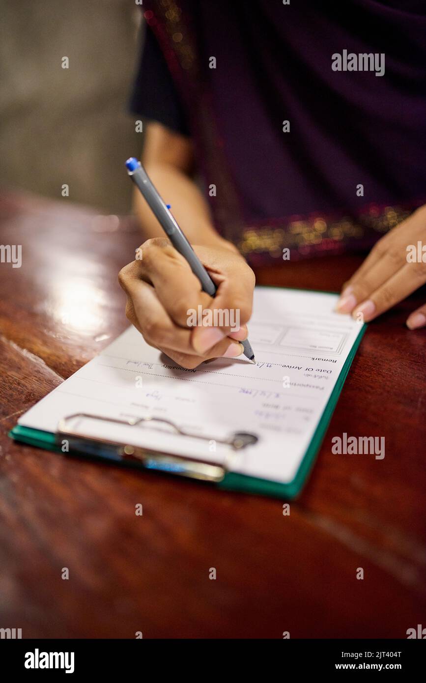 Checking in at the hotel. Closeup shot of a woman filling out a hotel ...