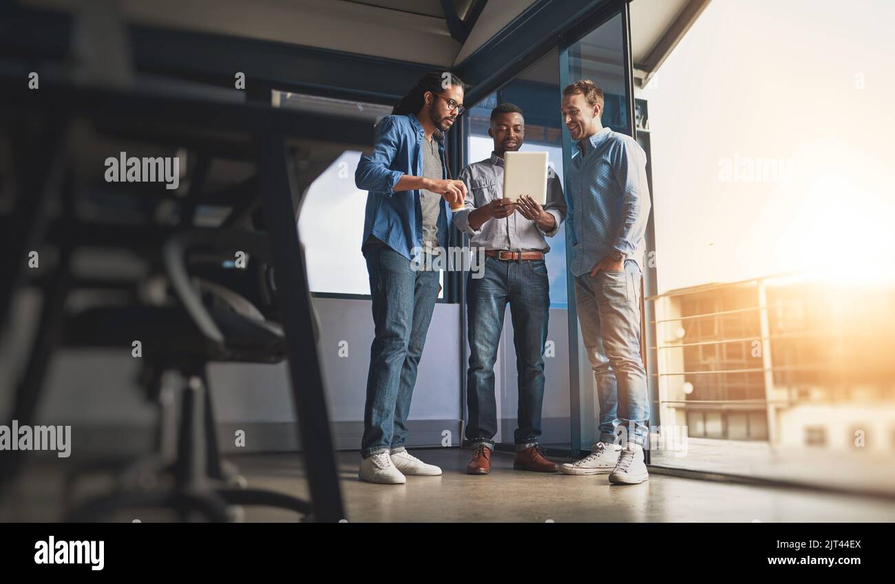 Threes company. three young designers talking over a digital tablet in ...