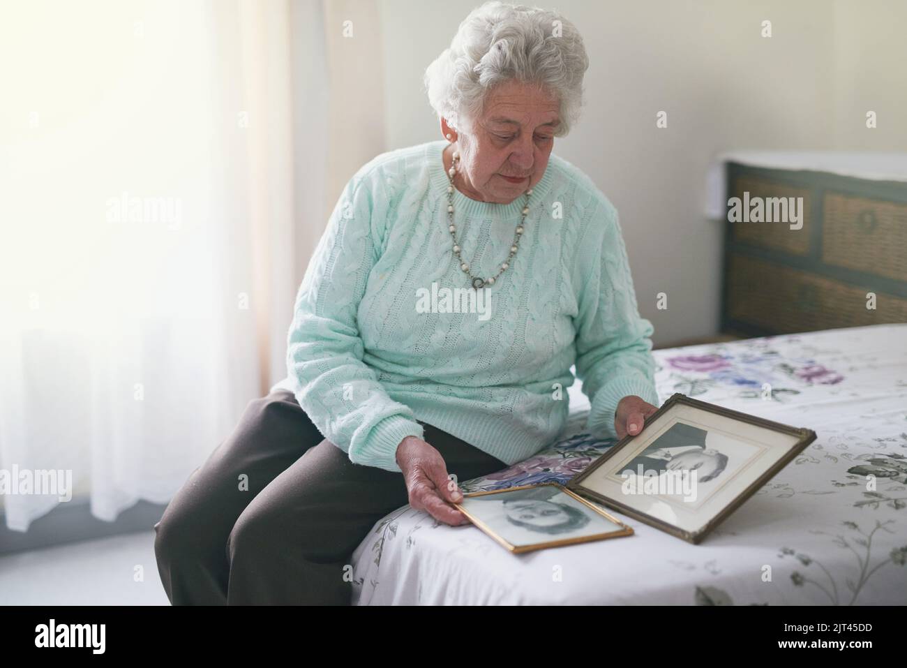 Remembering the good old days. a senior woman looking at old black and white photos of a man and ...