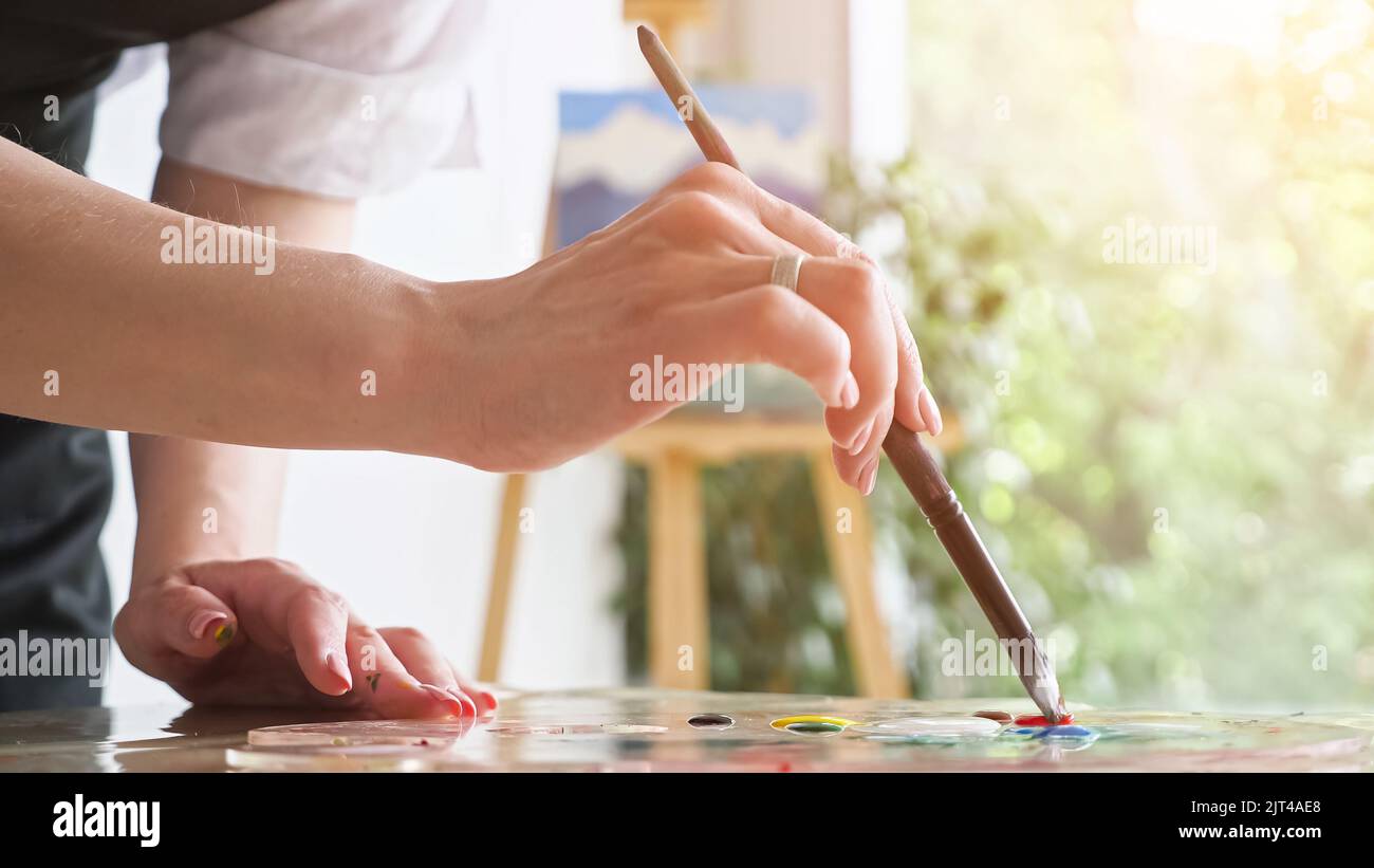Person hand mixes colours on palette against painting Stock Photo - Alamy