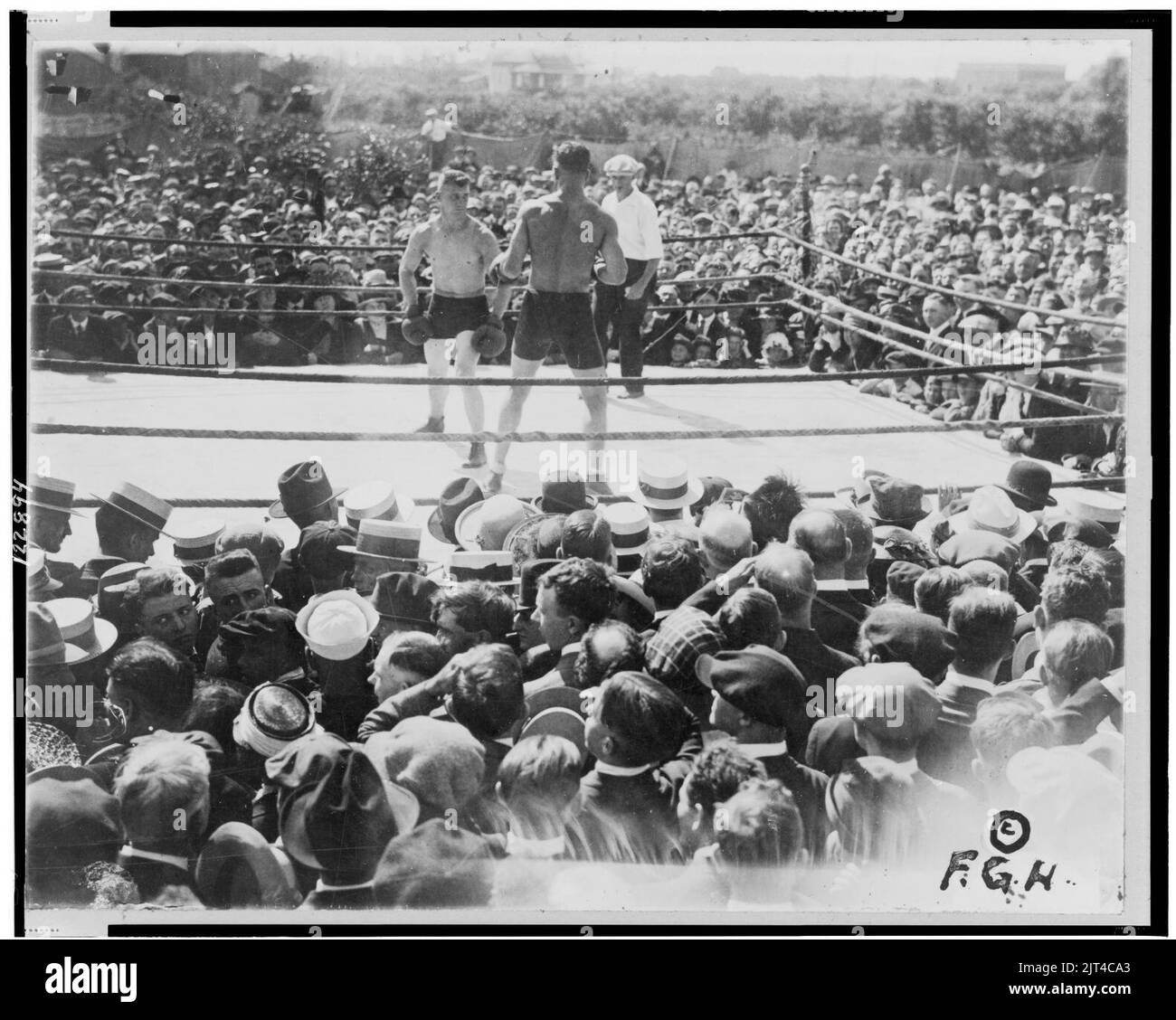 Two boxers and referee in outdoor boxing ring, surrounded by audience ...
