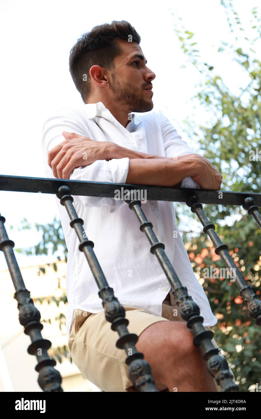 Attractive Spanish guy wearing white shirt is posing by the staircase ...