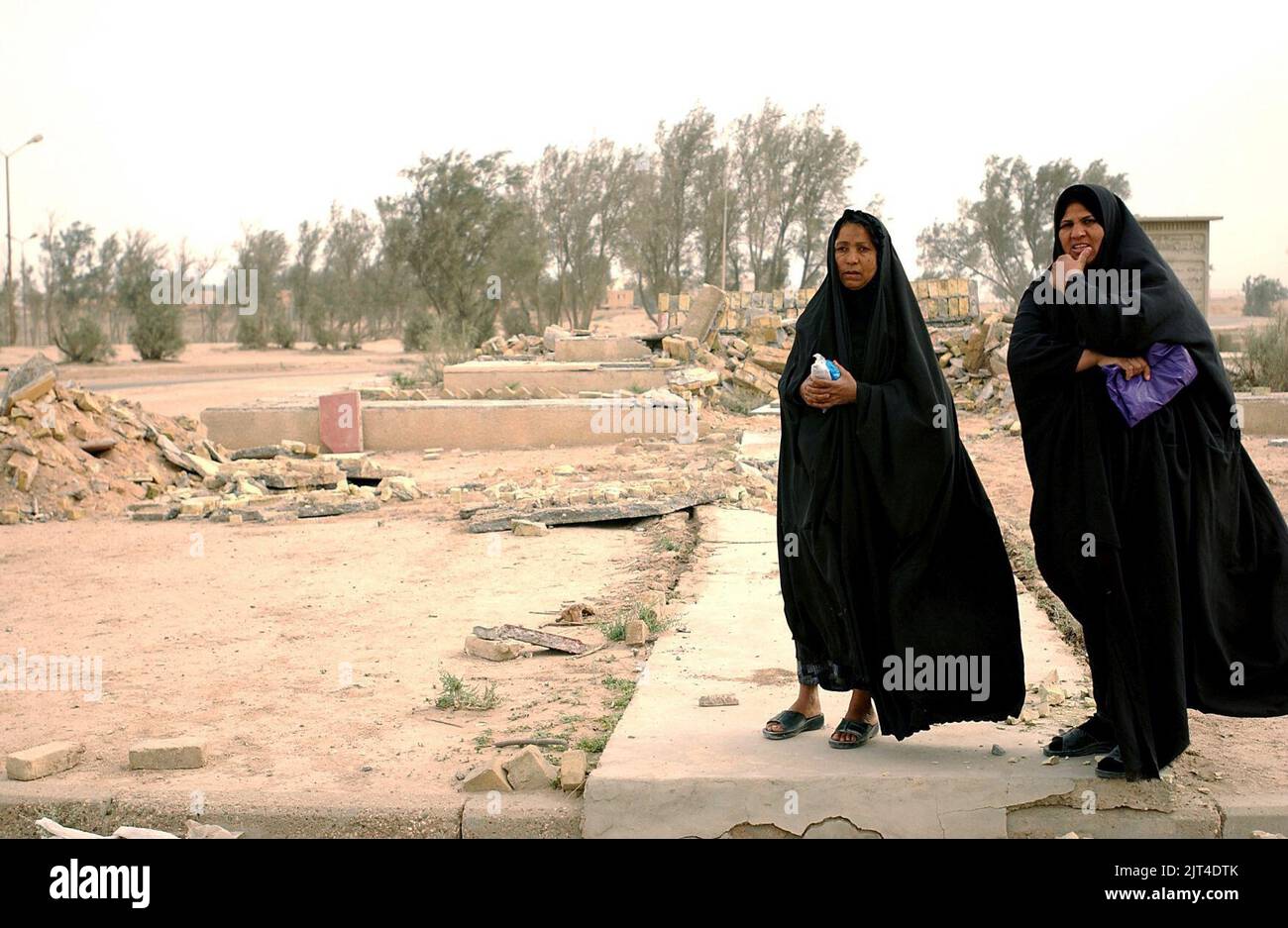 Two local Iraqi women pause to watch passing military convoys near the ...