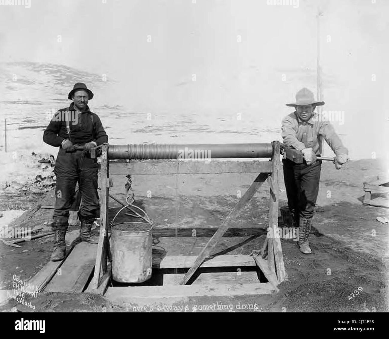 Two men operating a hand winch for hauling dirt from a mining shaft ...