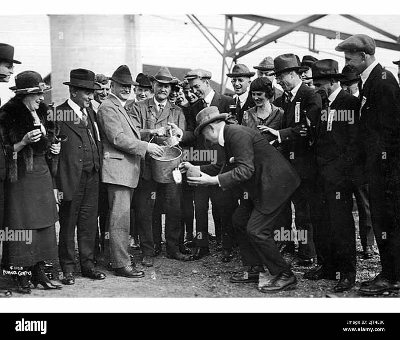 Two men with bucket of cider dispensing samples to group of men and ...