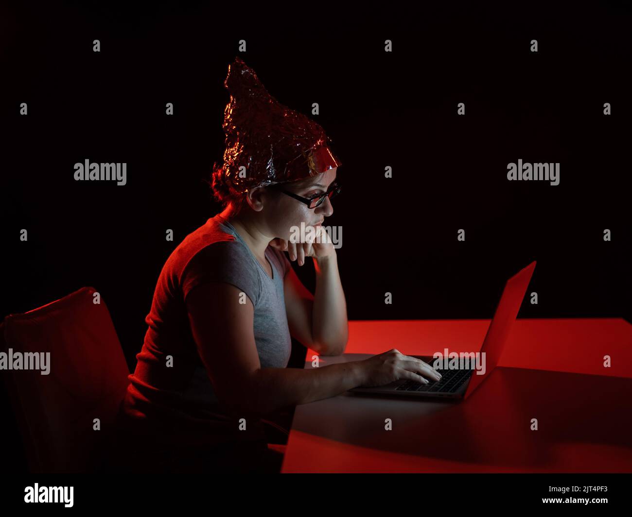 Paranoid caucasian woman typing on a computer wearing a tinfoil cap ...