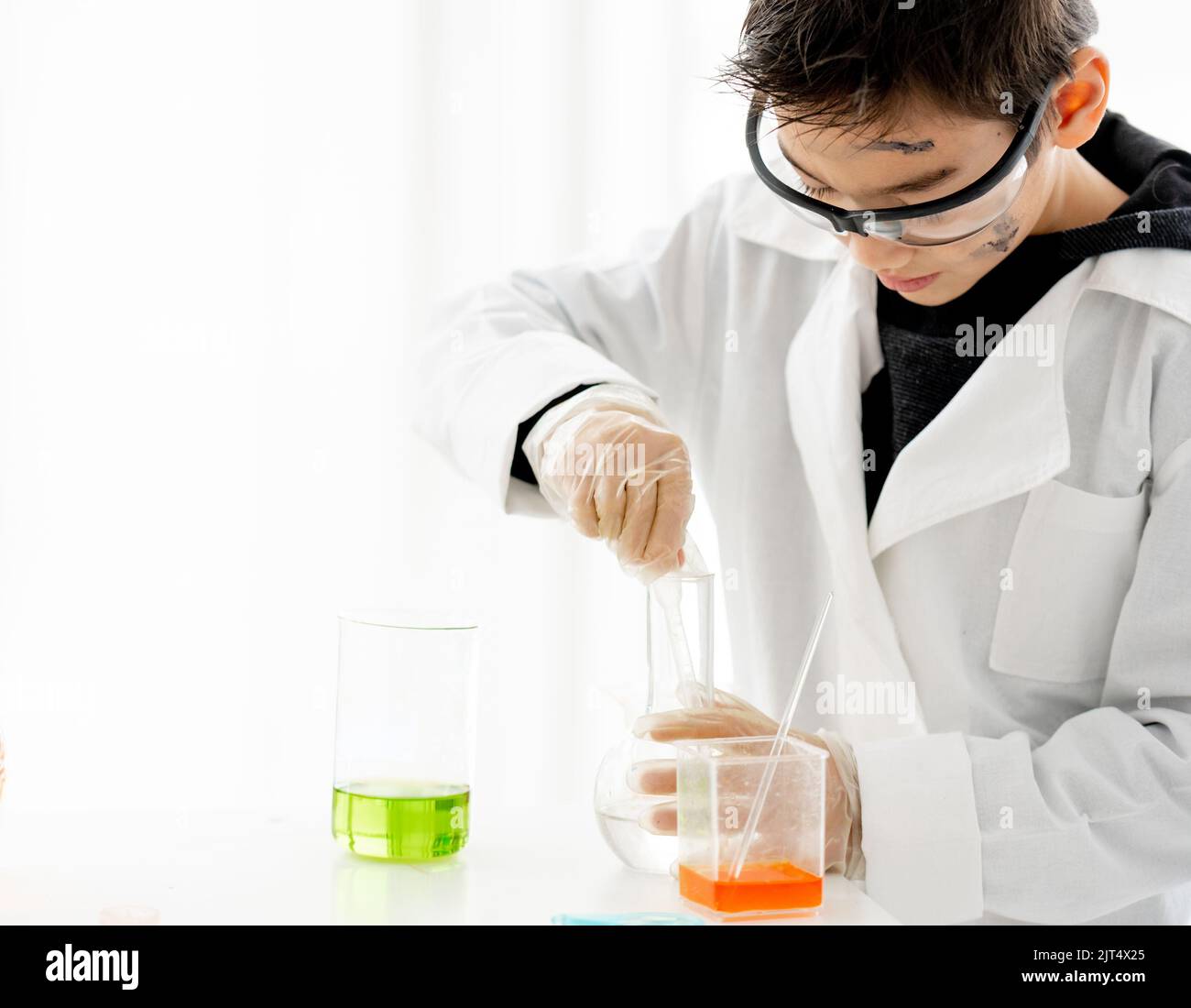 School boy doing chemistry experiment measuring chemical liquids in elementary science class ...