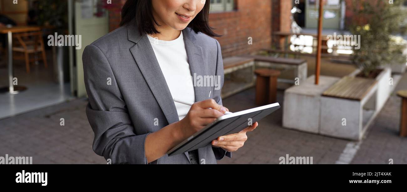 Happy professional woman taking notes using digital tablet standing ...