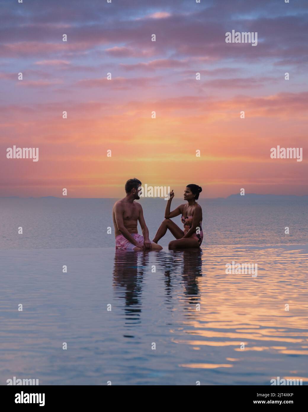 couple men and women relaxing on the edge of a pool during sunset by ...