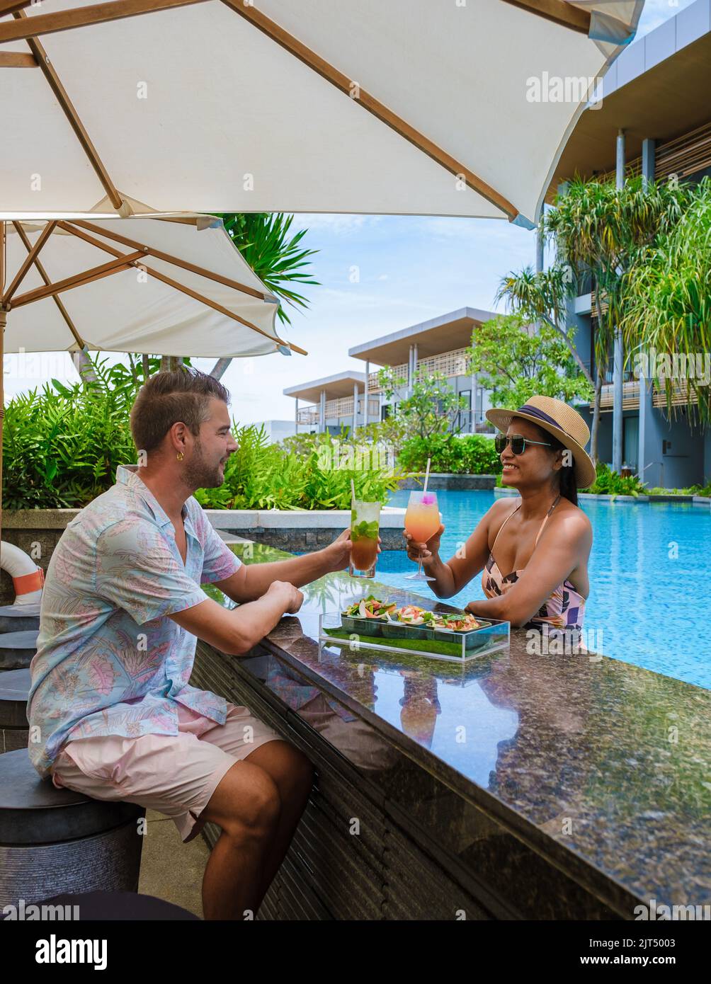 Couple sitting on the bar in a swimming pool drinking cocktails, eating ...