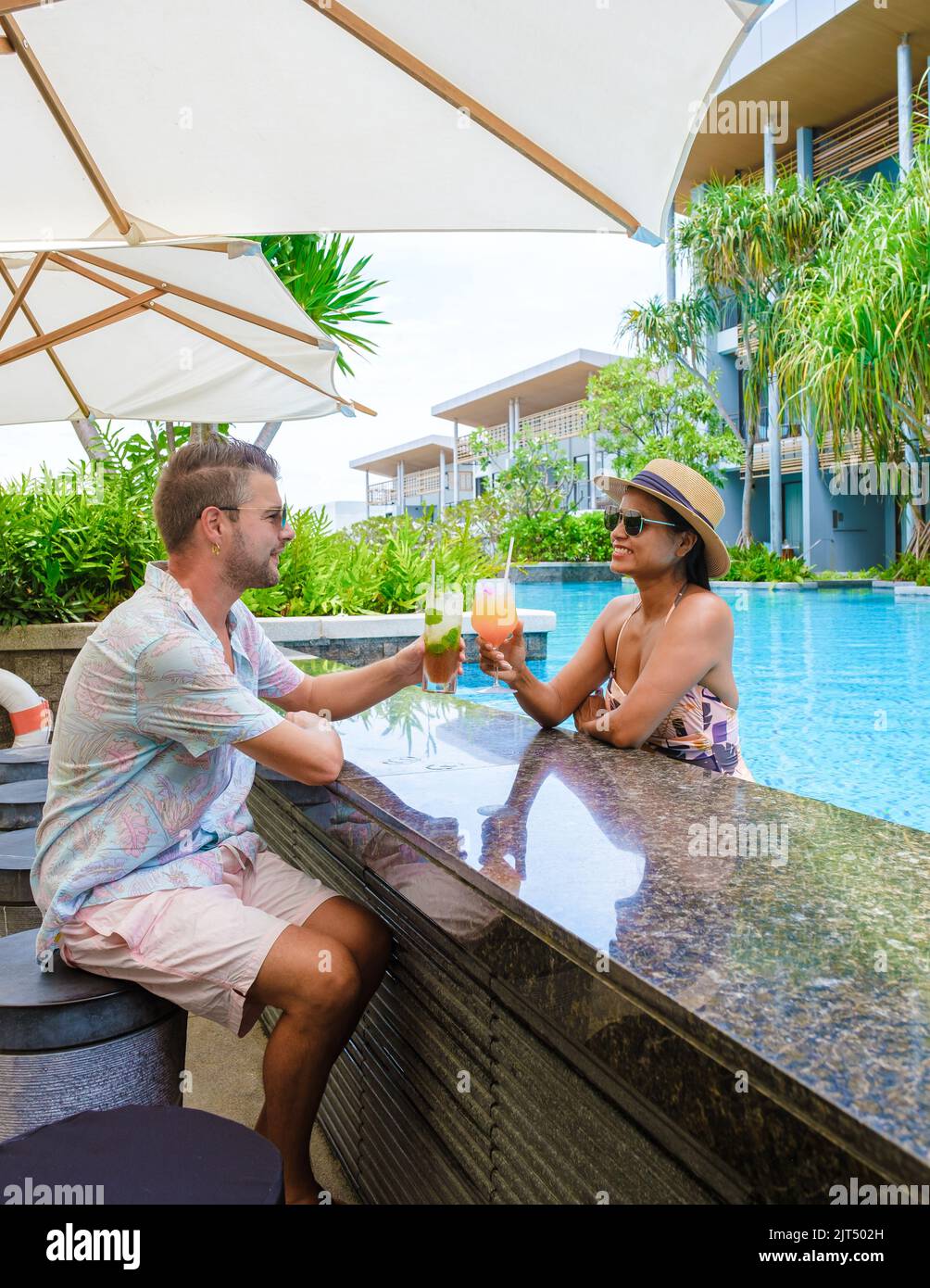 Couple sitting on the bar in a swimming pool drinking cocktails, eating ...
