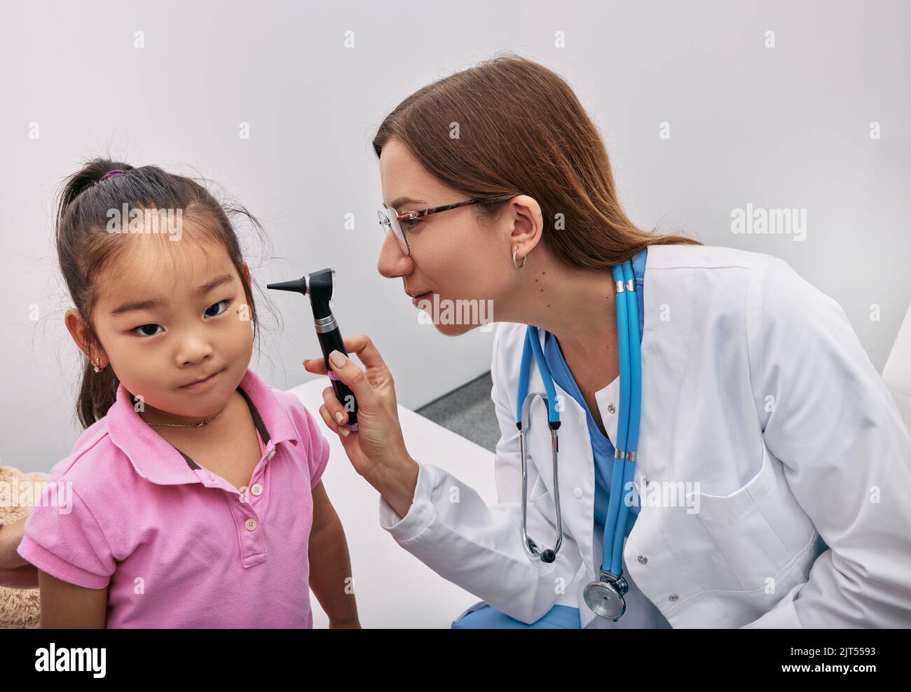 Caucasian pediatrician examining Japanese girl with otoscope, hearing ...