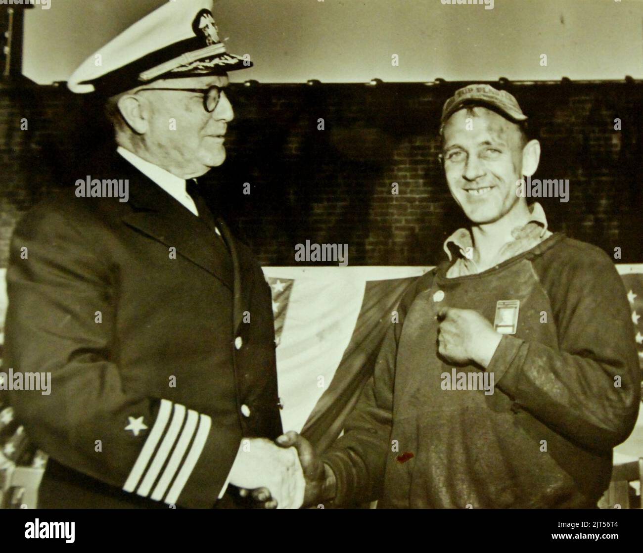 U.S. Navy CPT Robert Henderson presents a Navy “E” button to brass ...
