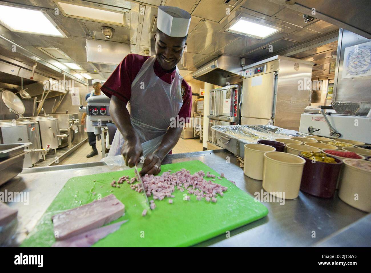 U.S. Navy Culinary Specialist Seaman chops ham in the galley of the ...