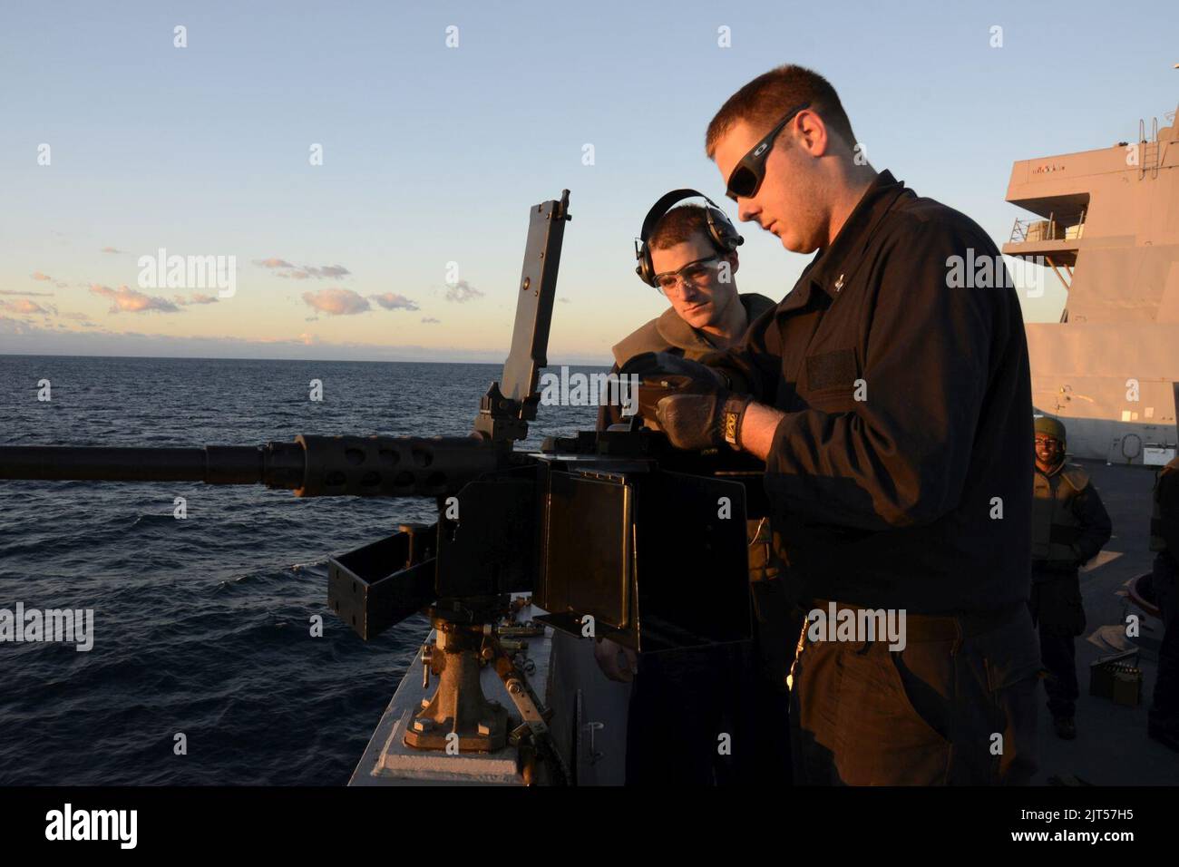 U.S. Navy Gunner's Mate 2nd Class foreground, demonstrates how to load ...