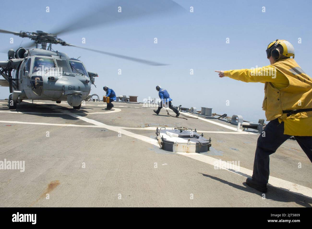 U.S. Navy Lt. j.g. signals Sailors to chock and chain an MH-60S Seahawk ...