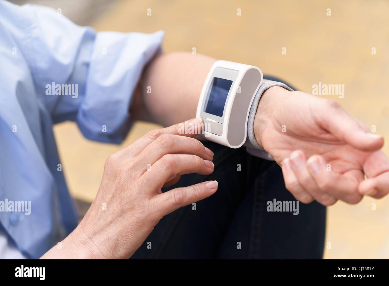 Mature woman use arm pulse, blood pressure monitor sitting outside ...