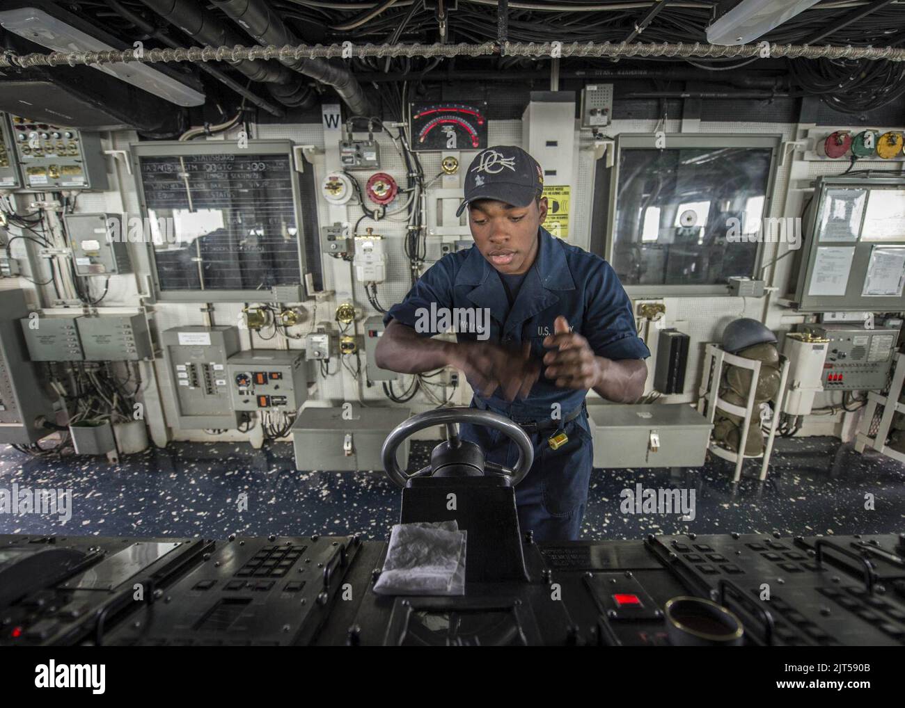U.S. Navy Seaman steers the ship while standing helmsman watch aboard ...