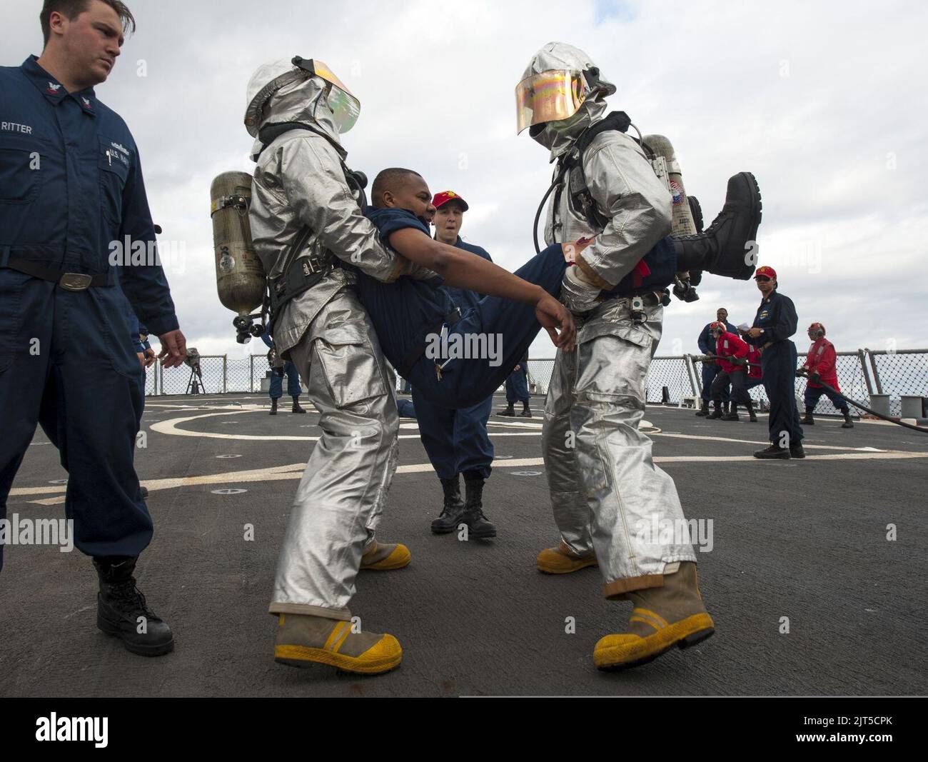U.S. Sailors wearing firefighting proximity suits carry a simulated ...