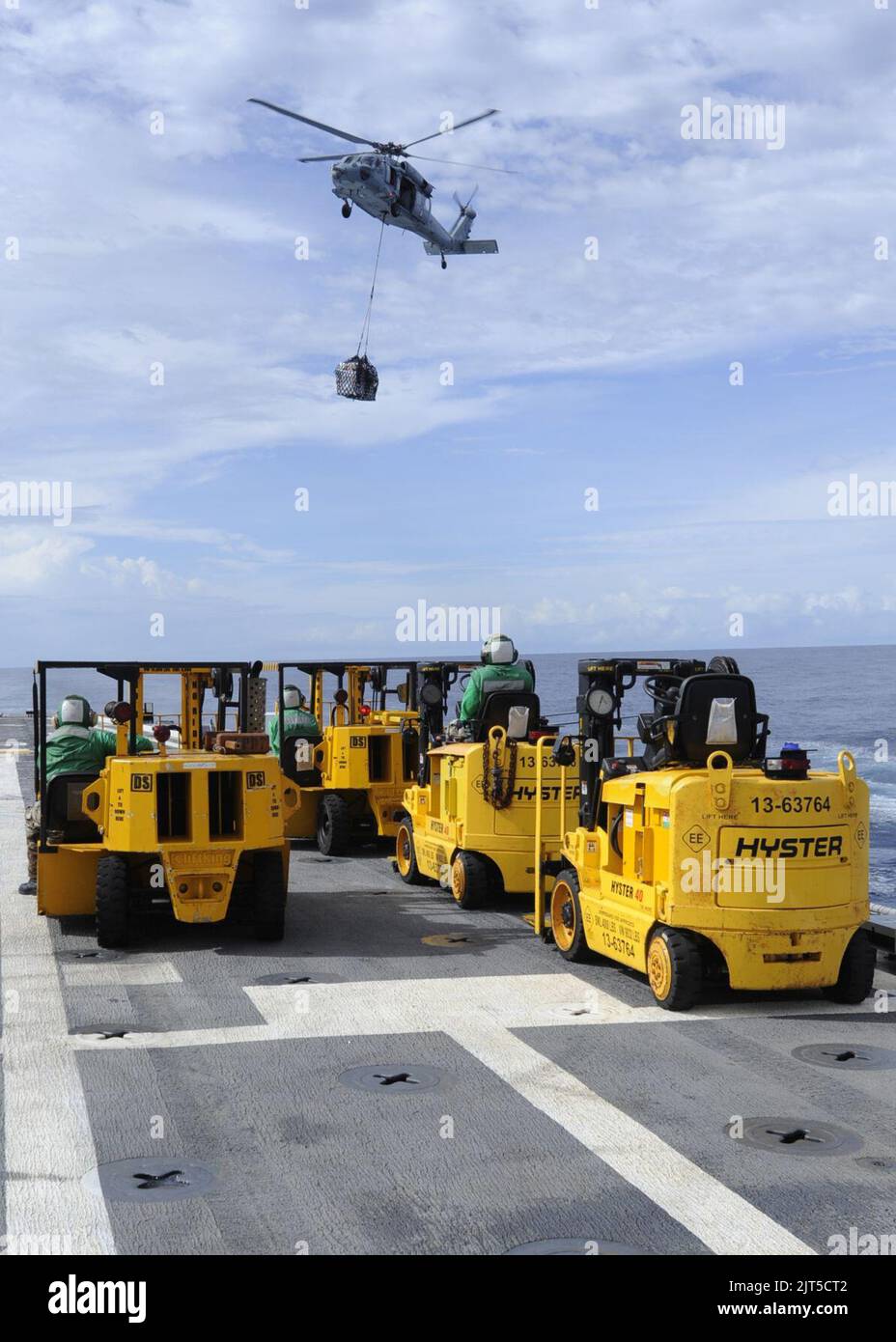 U.S. Sailors with forklifts stand by to move cargo as a Navy MH-60S ...