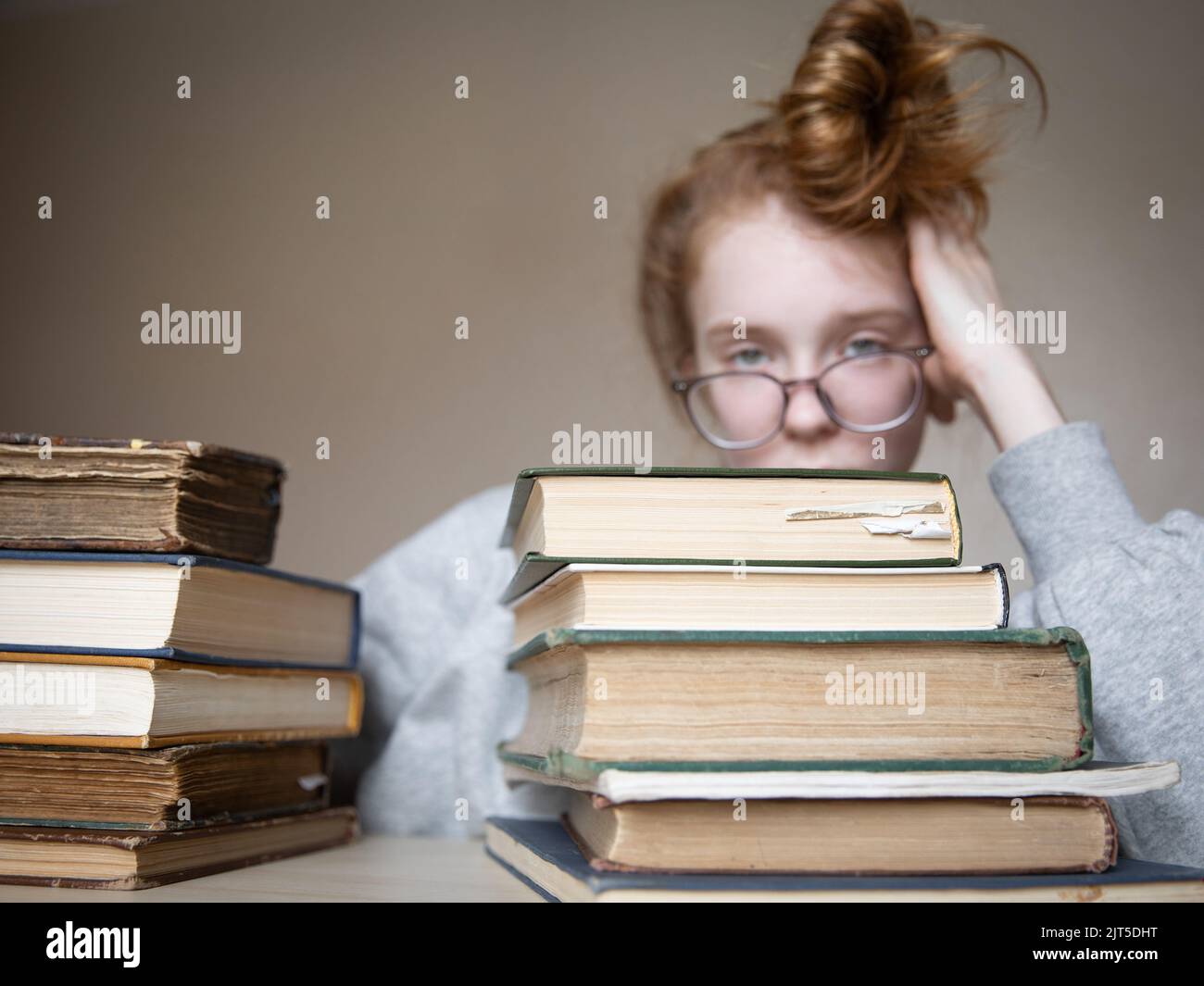 The focus is on two large piles of books on the table. A tired girl ...