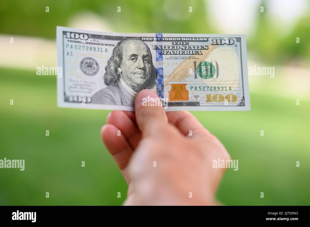 Close up 100 Dollar bank note in hand on grass background. One hundred ...
