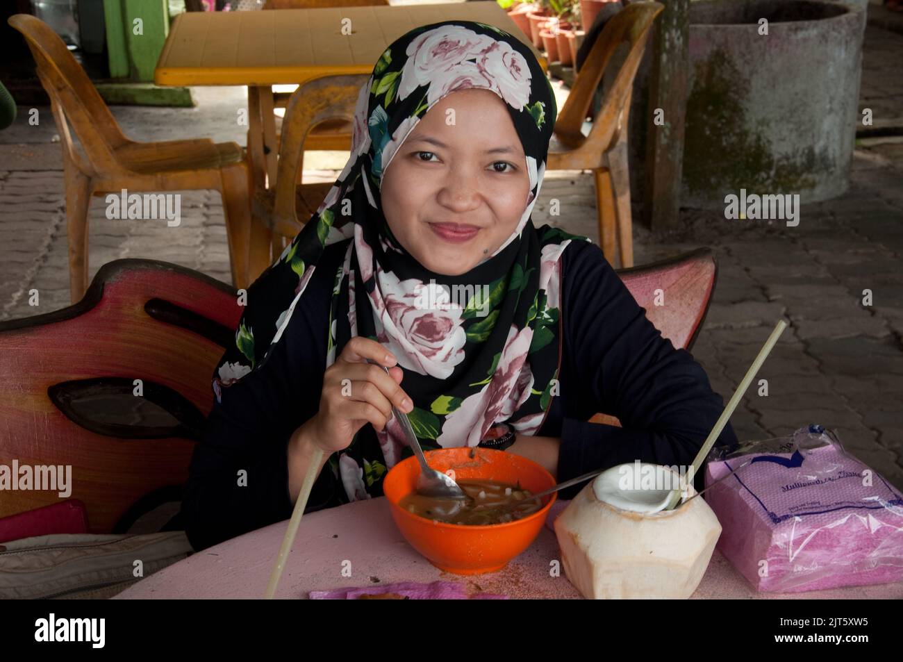 Young Muslim Woman eating Laksa in open-air cafe, Batu Ferringhi ...