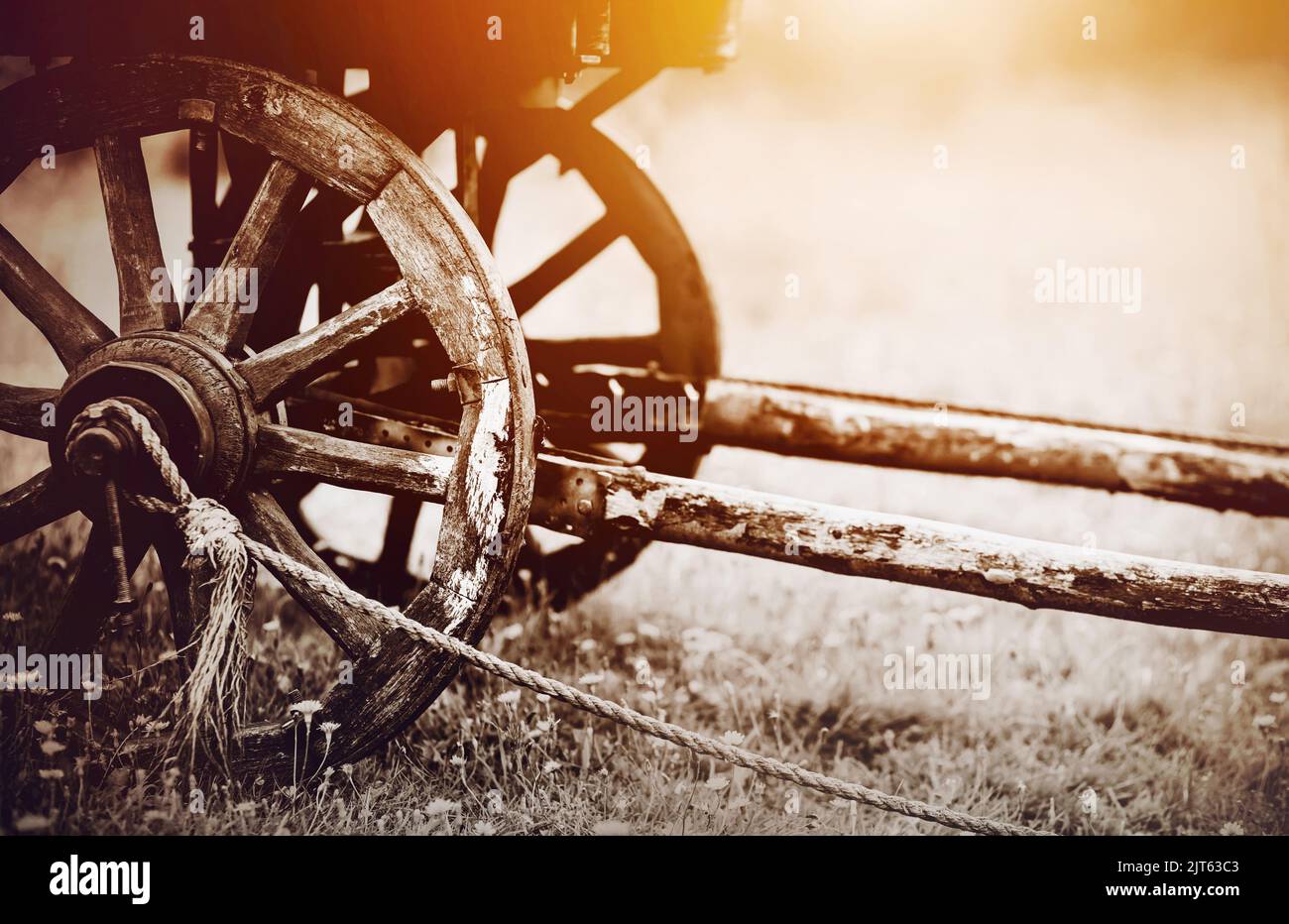 An old retro wooden cart with big wheels stands in a field, illuminated ...