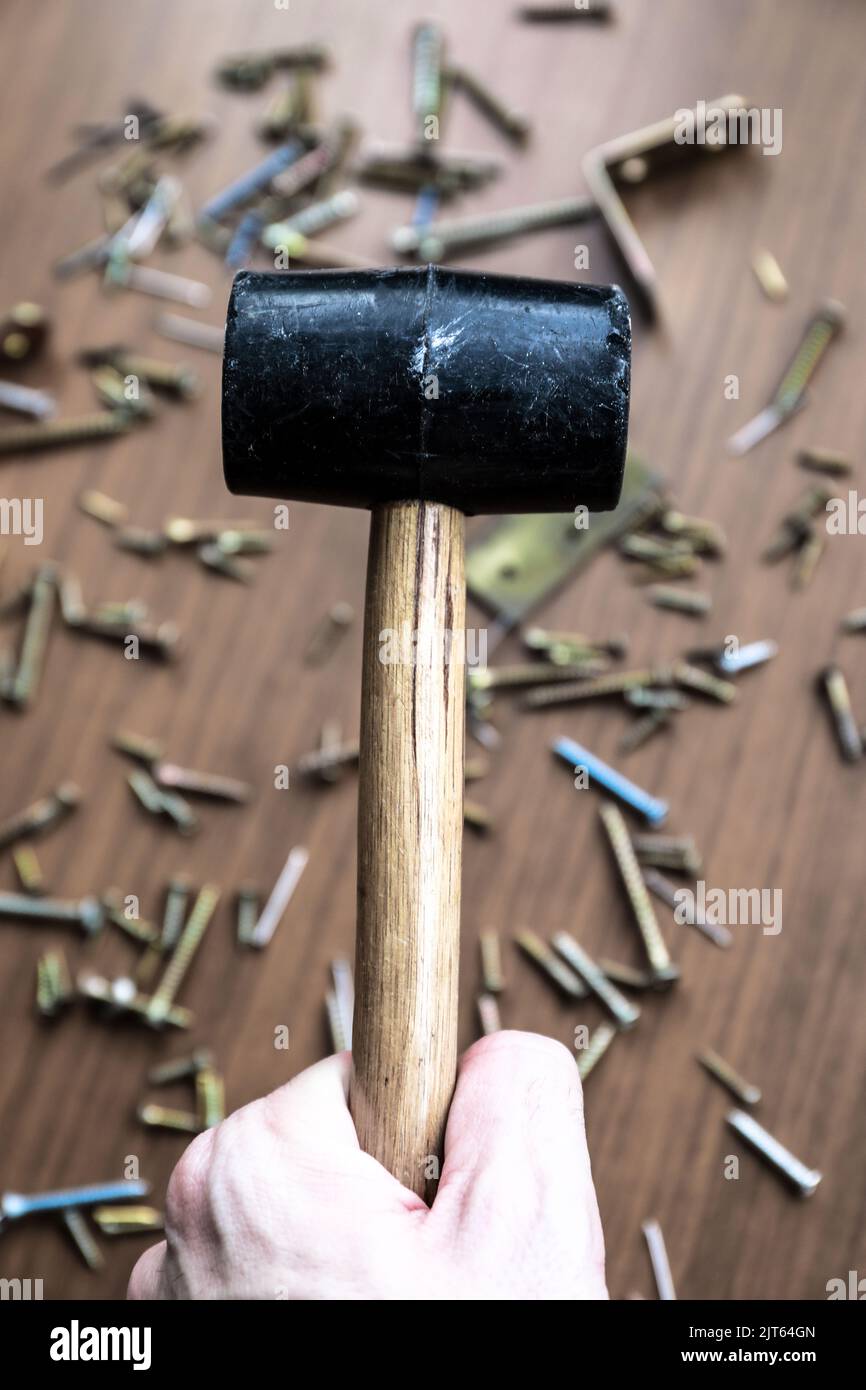 A vertical shot of a rubber mallet in a hand with screws on a wooden ...