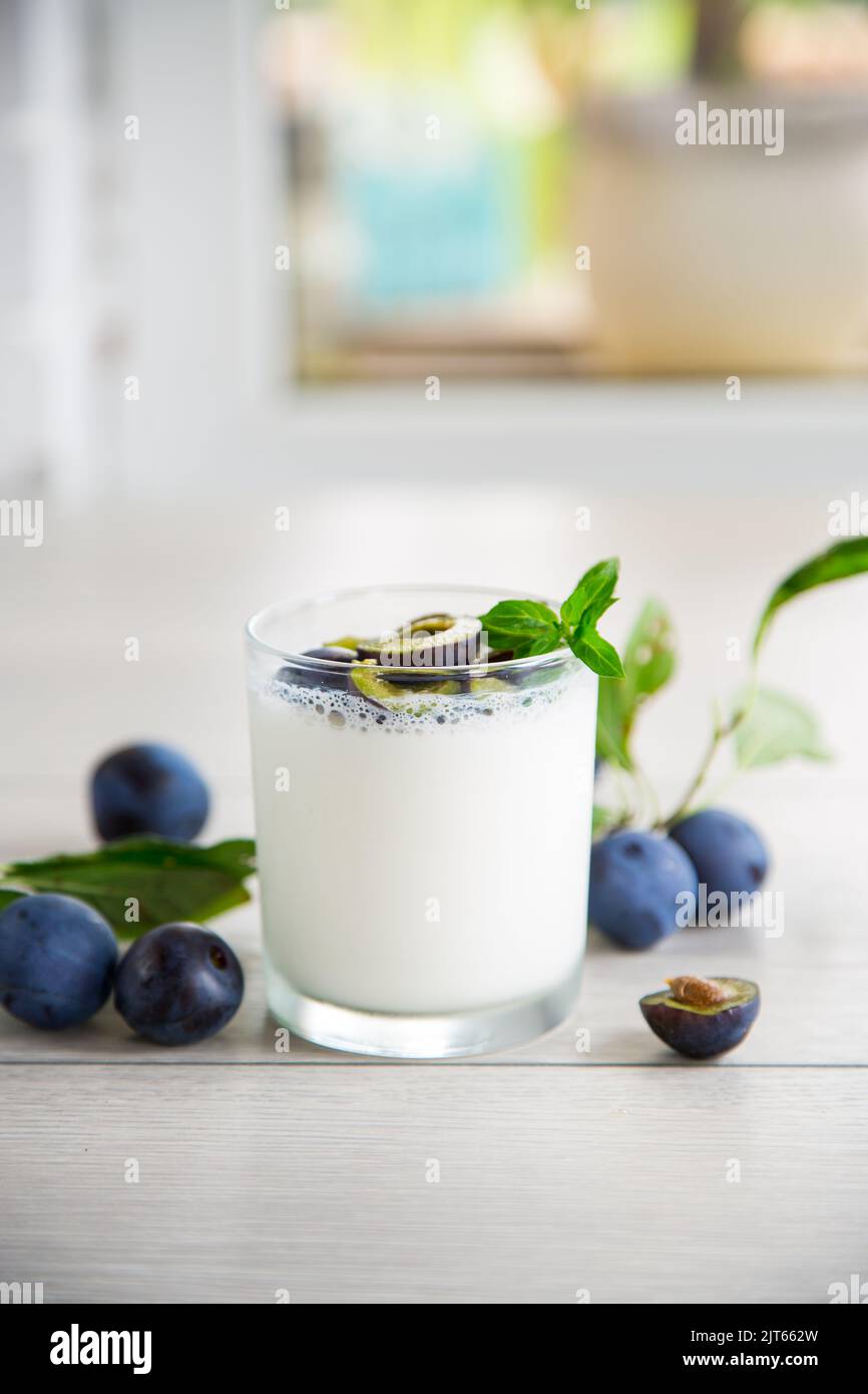 sweet homemade yogurt with fresh plum slices in a glass on a wooden ...