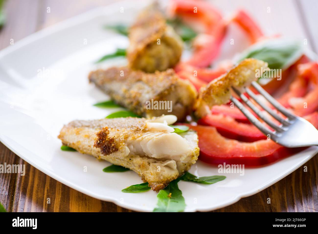 Pieces of fried hake fish in a plate with pepper on a wooden table ...