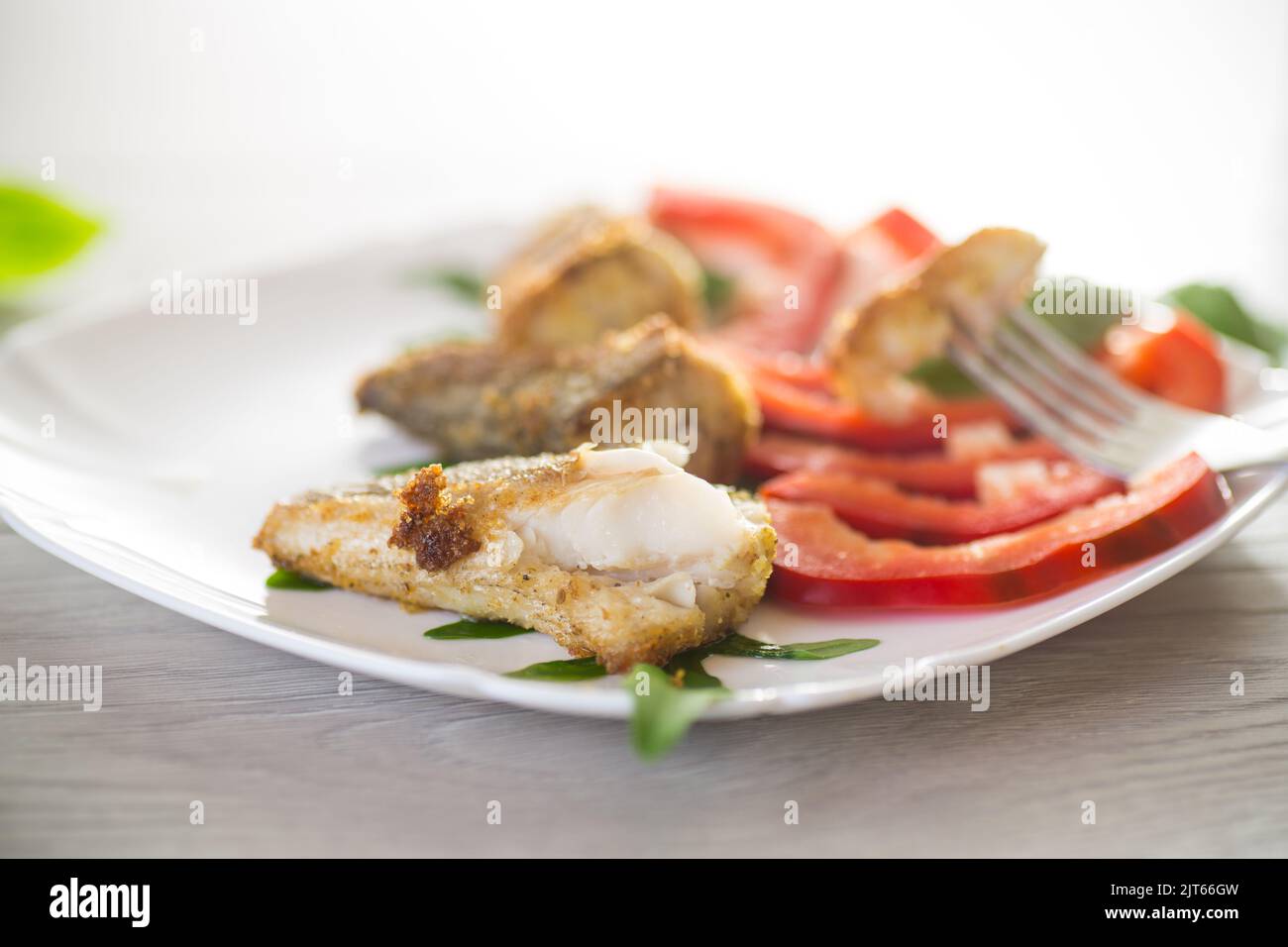 Pieces of fried hake fish in a plate with pepper on a wooden table ...