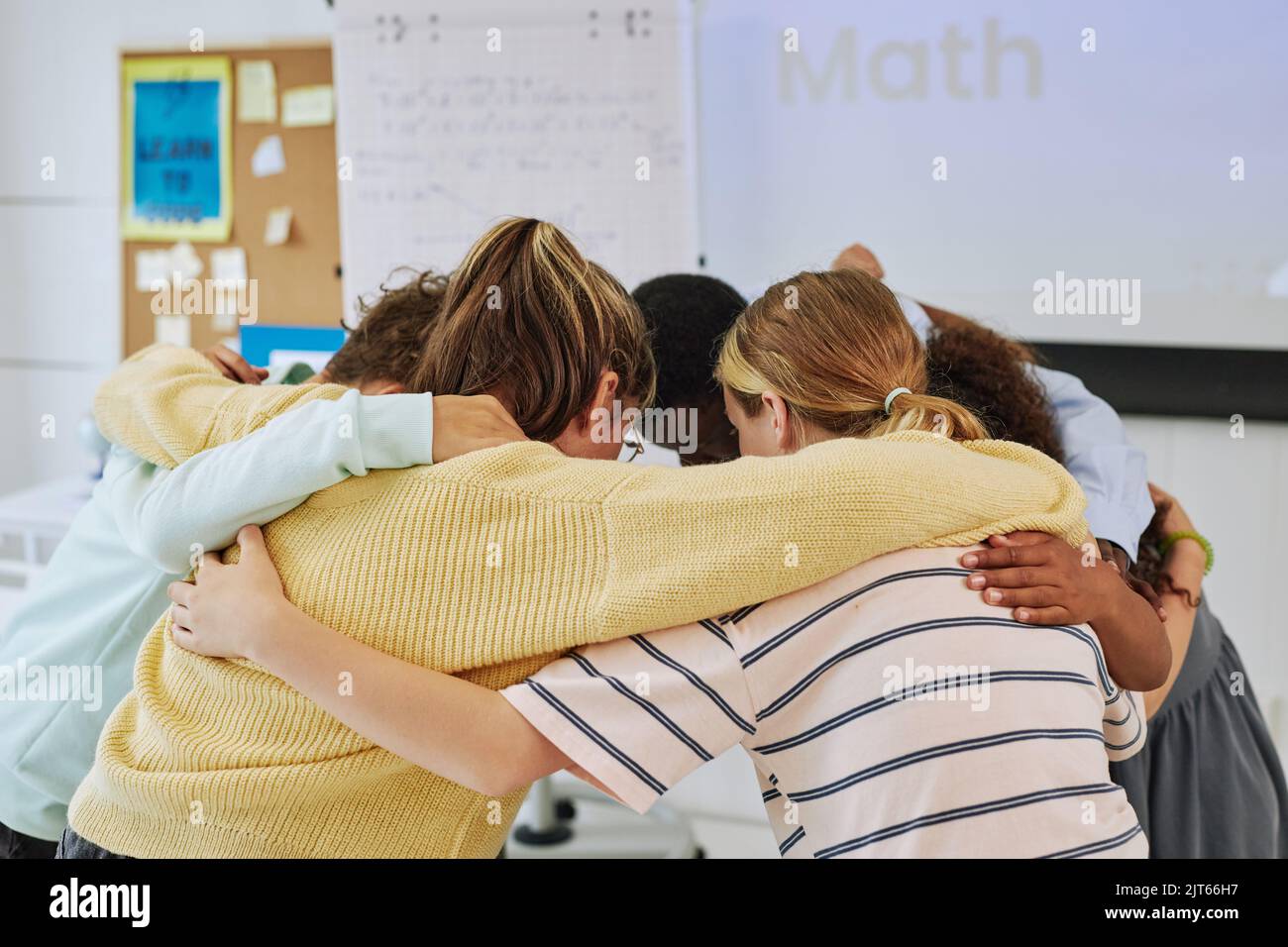 Diverse group of schoolchildren huddling in team exercise in classroom ...
