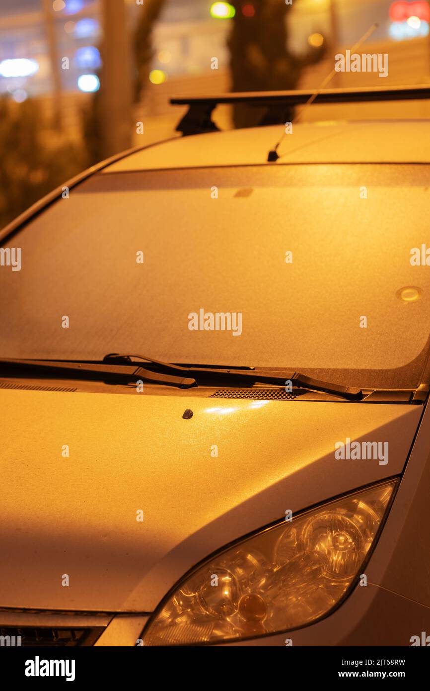 Misted car windshield at night. A parked silver car is covered with a ...