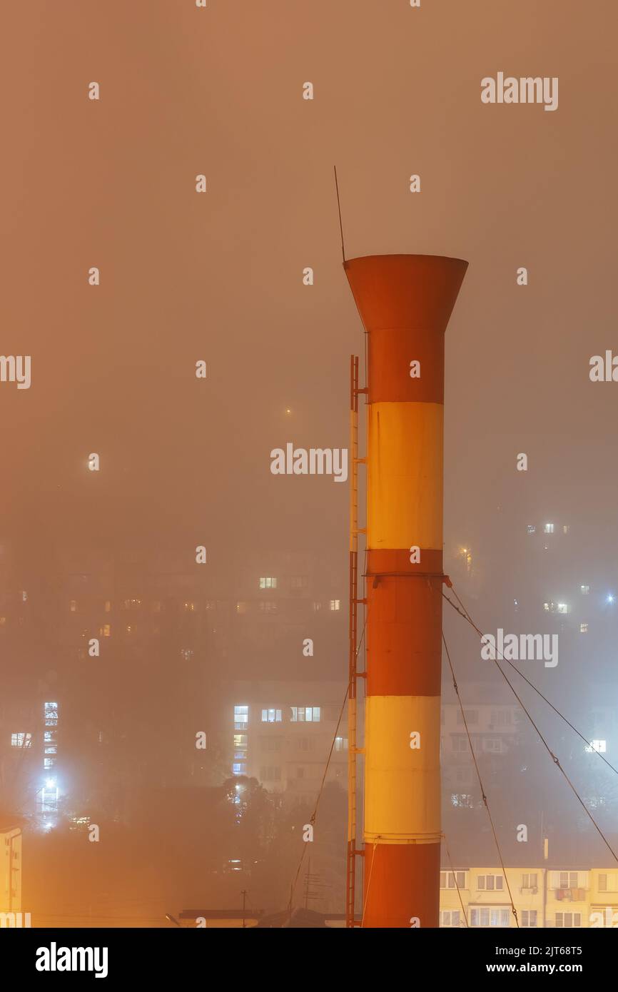 Red-white chimney of a boiler room against the background of windows of ...